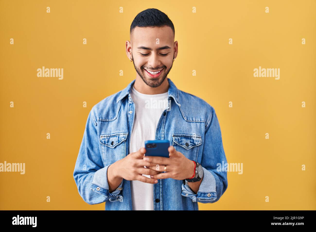Young hispanic man using smartphone typing message smiling with a happy ...