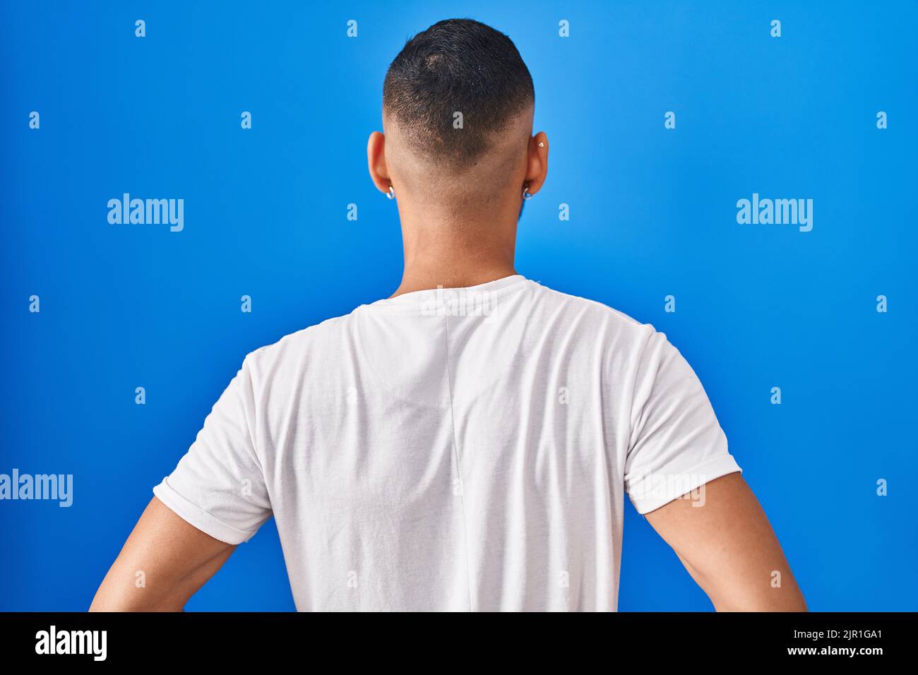 Young hispanic man standing over blue background standing backwards ...