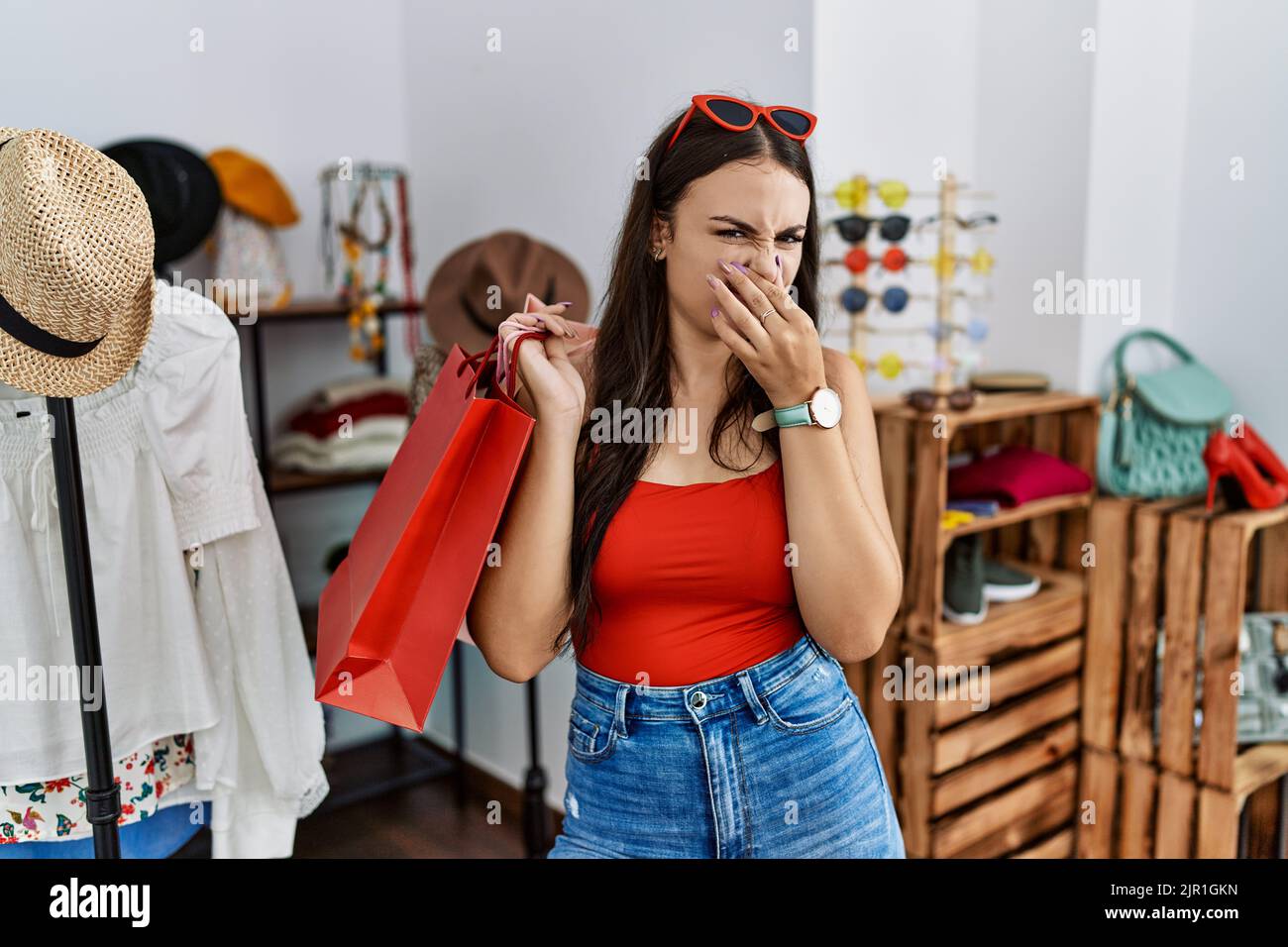 Young brunette woman holding shopping bags at retail shop smelling ...