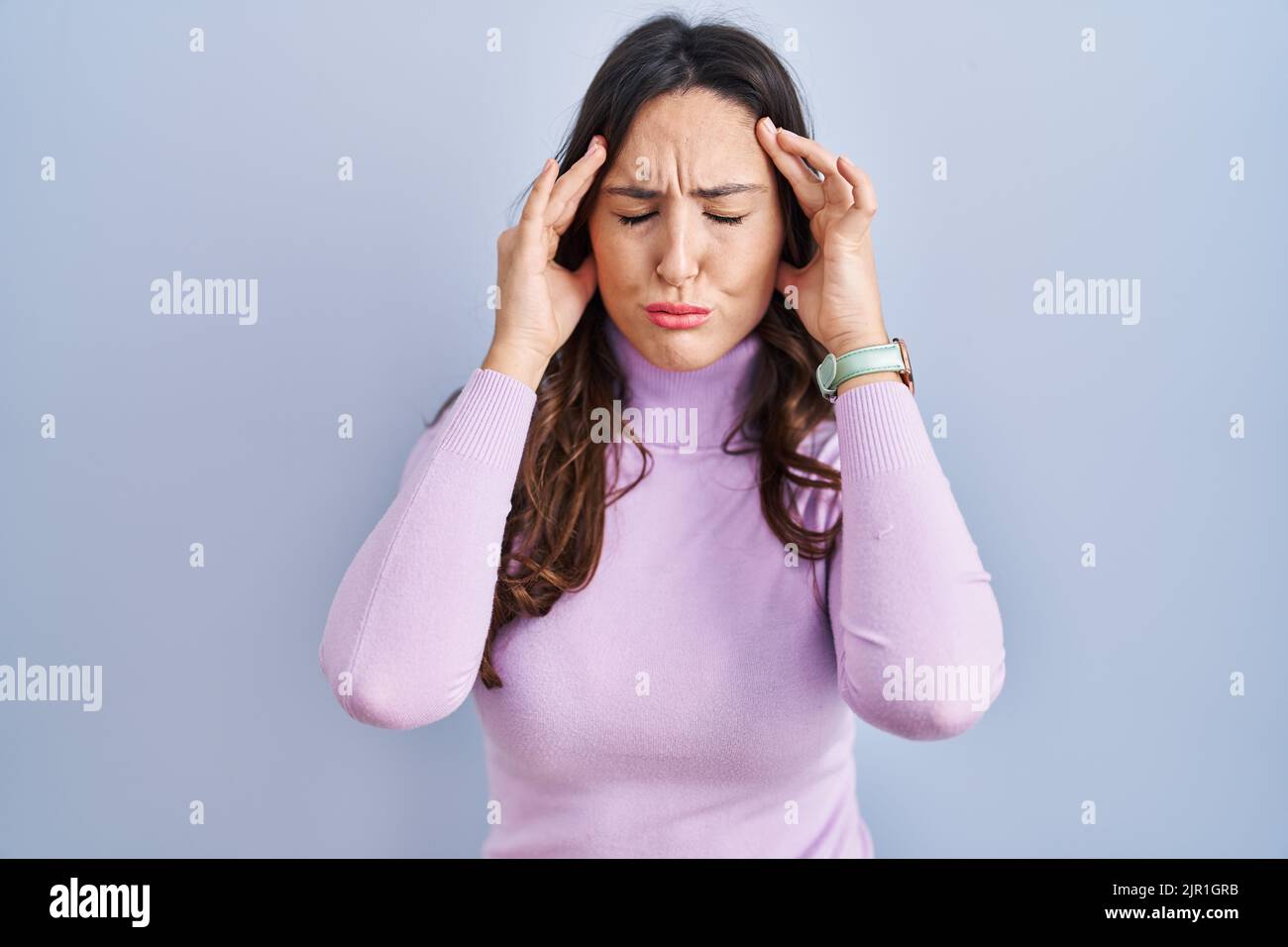 Young brunette woman standing over blue background with hand on head ...