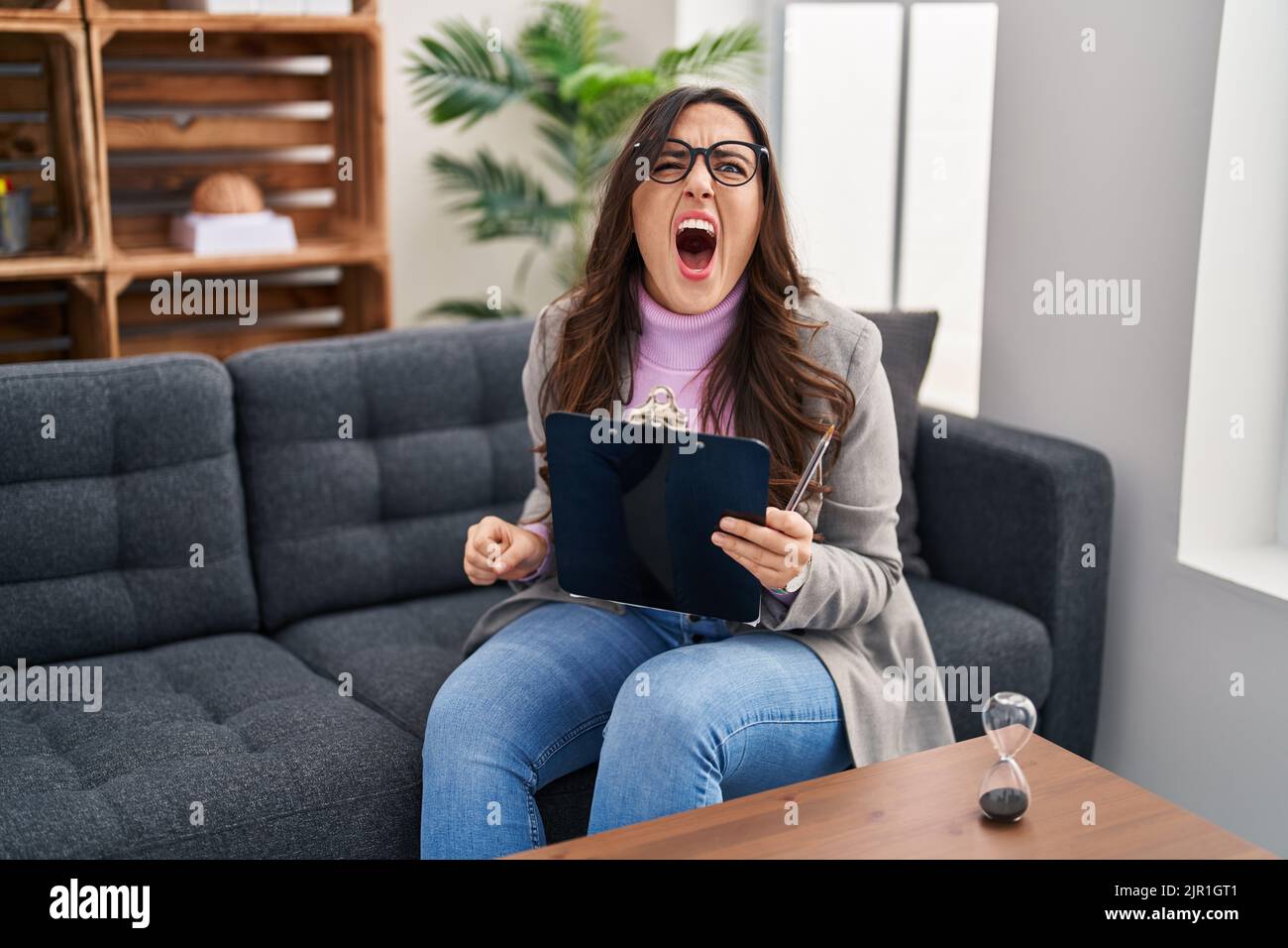 Young brunette woman working at consultation office angry and mad ...