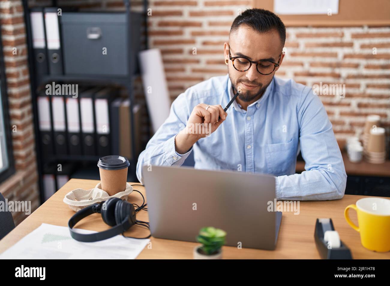 Young hispanic man business worker using laptop with doubt expression ...