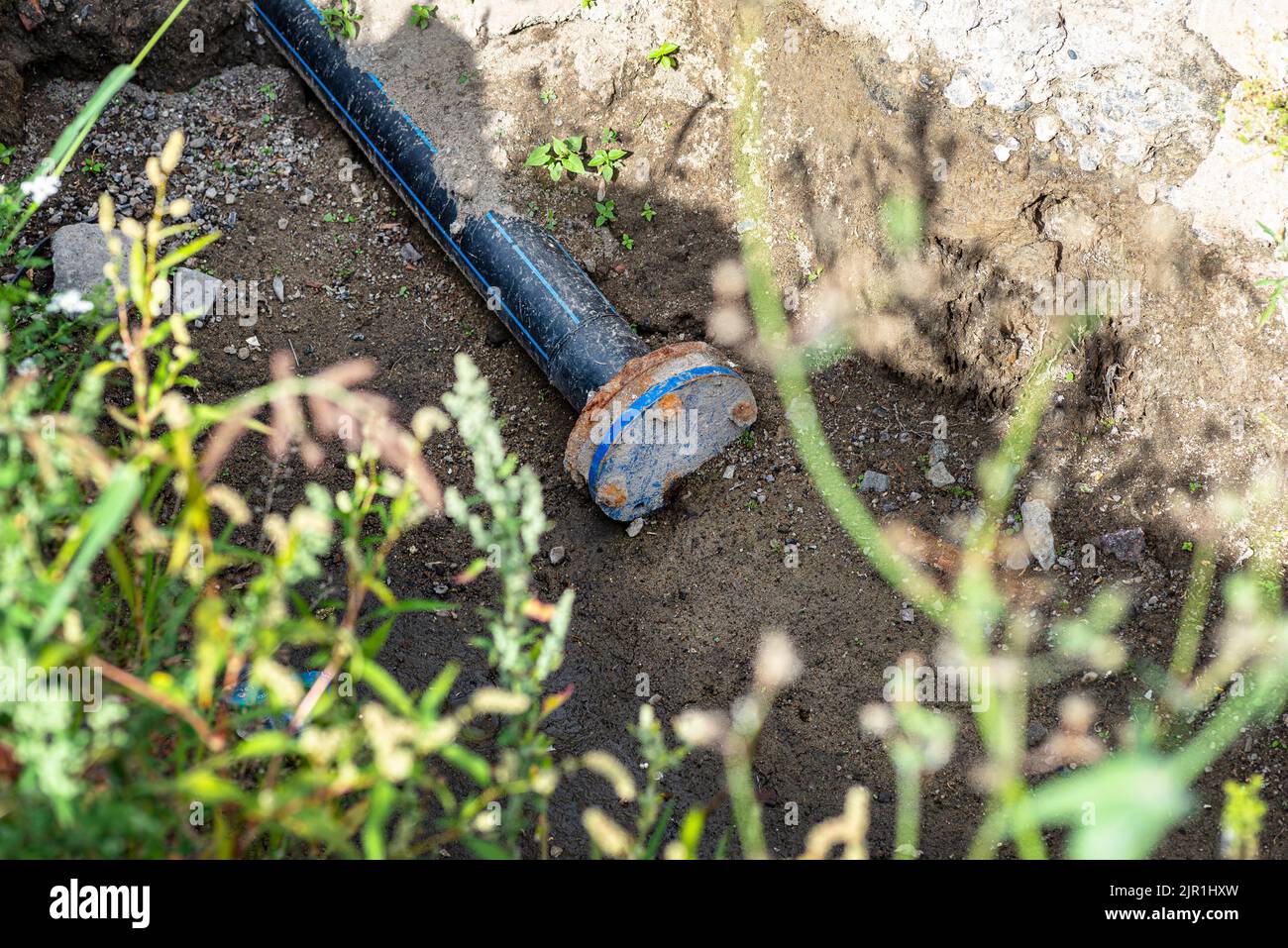 Closed end of a plastic water pipe lying along a ditch with high ...
