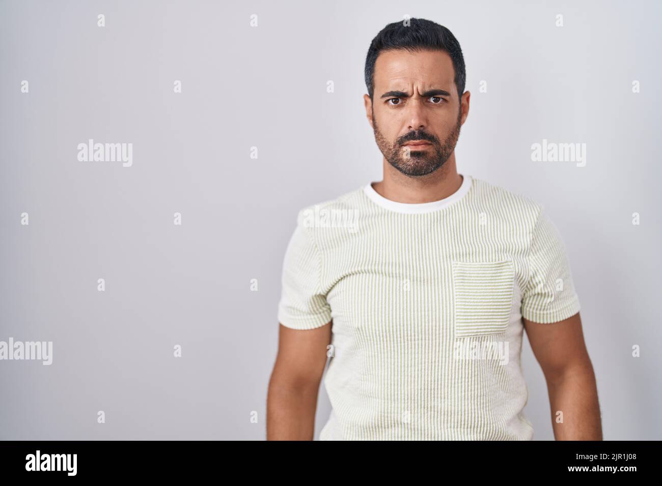 Hispanic man with beard standing over isolated background skeptic and ...