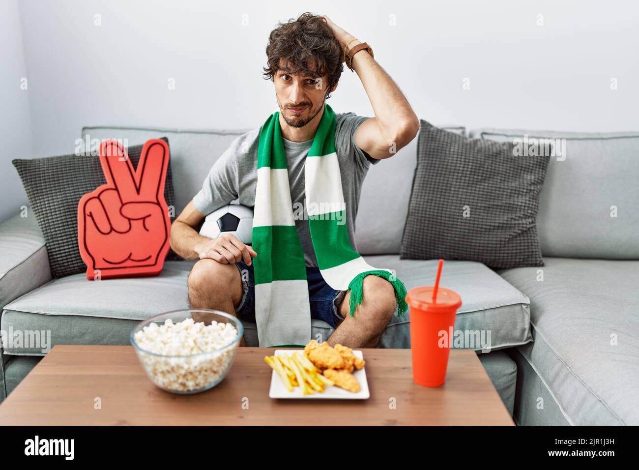 Young hispanic man football hooligan cheering game at home confuse and ...