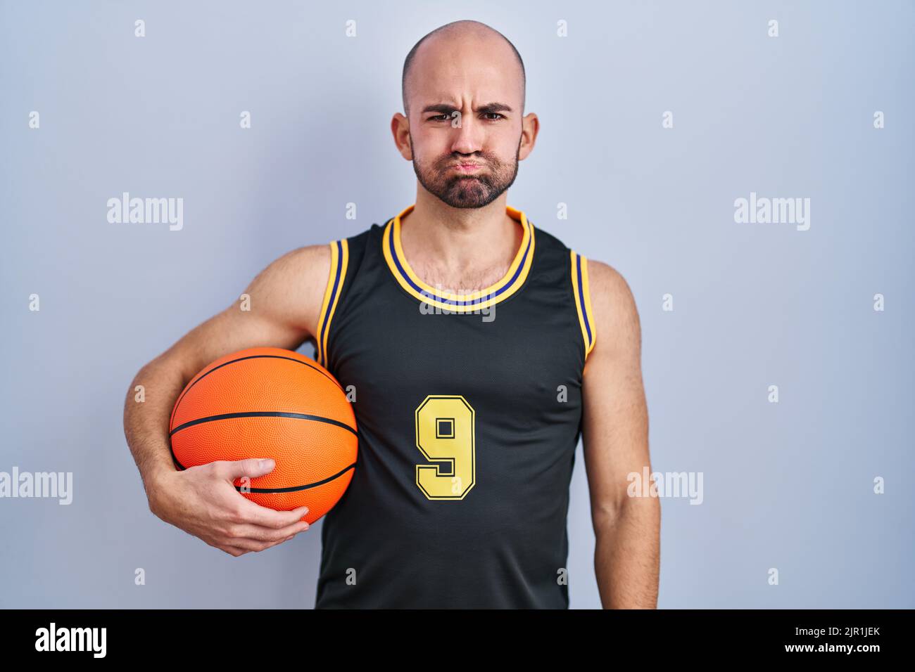 Young bald man with beard wearing basketball uniform holding ball ...