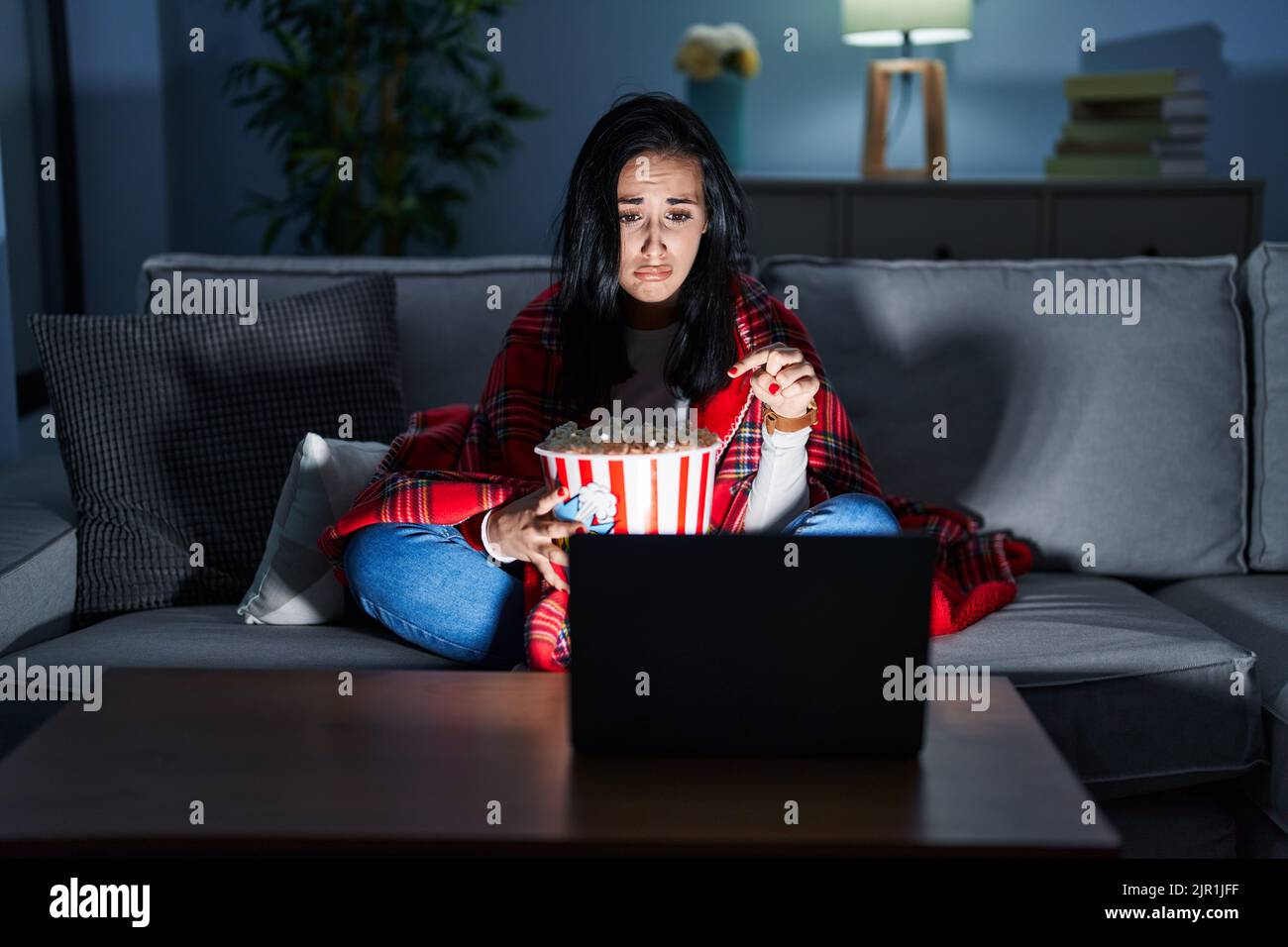 Hispanic woman eating popcorn watching a movie on the sofa pointing ...