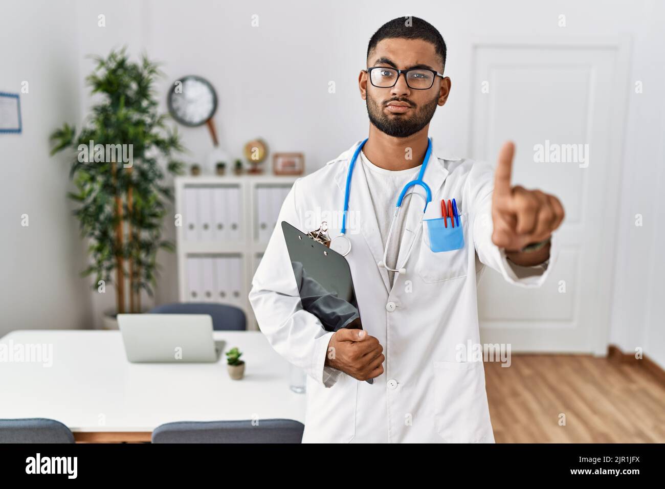 Young indian man wearing doctor uniform and stethoscope pointing with ...