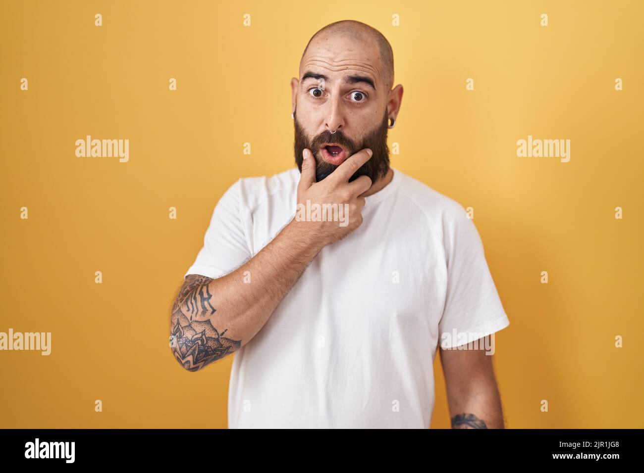Young hispanic man with beard and tattoos standing over yellow ...