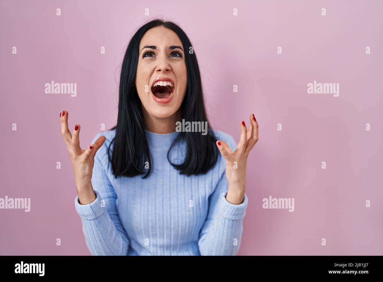 Hispanic woman standing over pink background crazy and mad shouting and ...