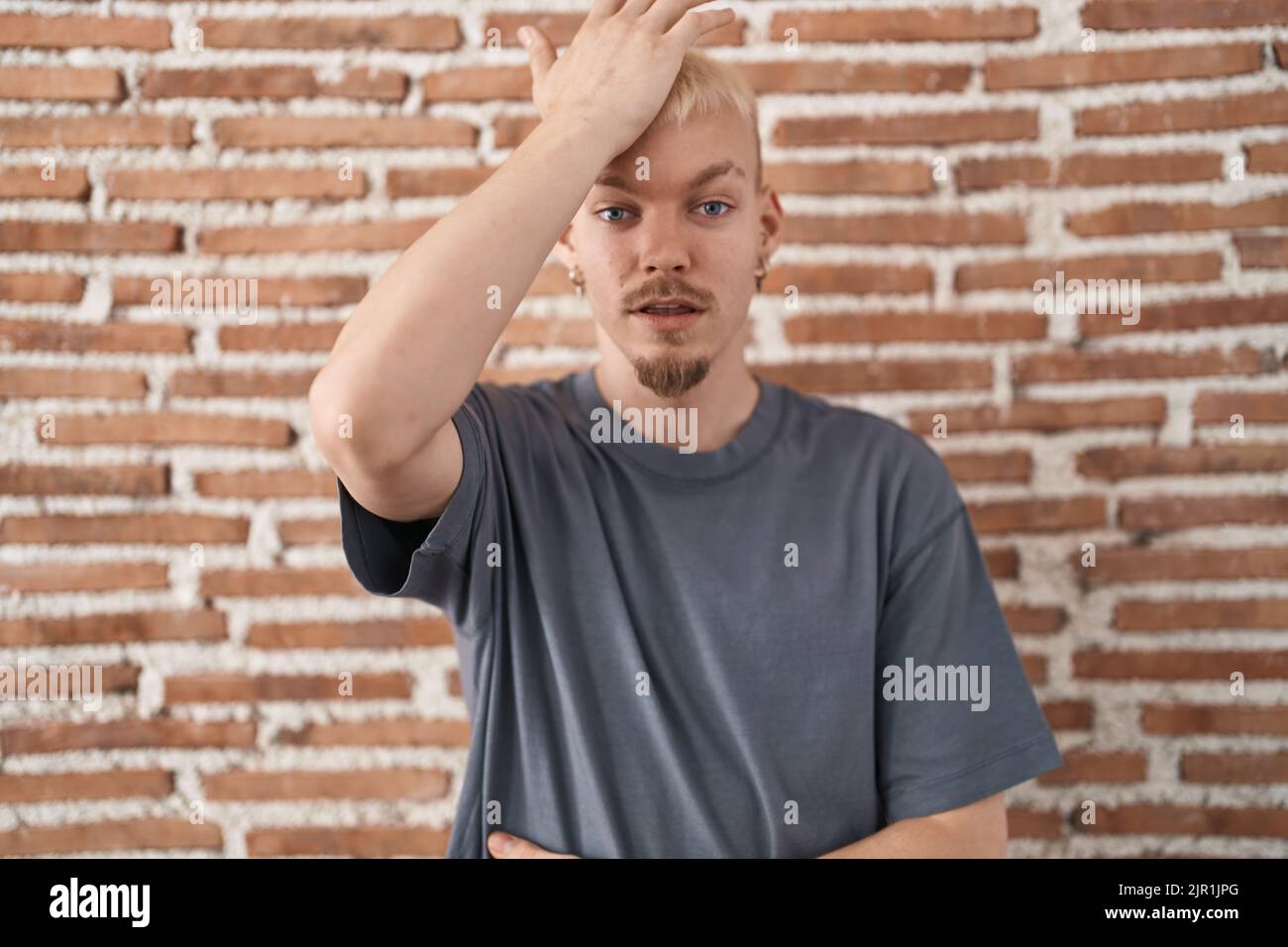 Young caucasian man standing over bricks wall surprised with hand on ...