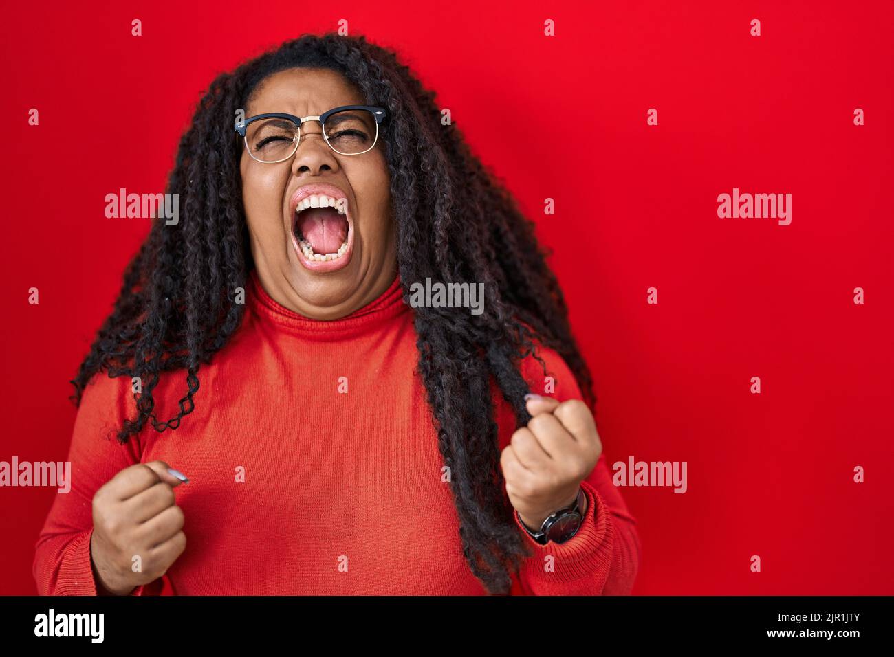 Plus size hispanic woman standing over red background angry and mad ...