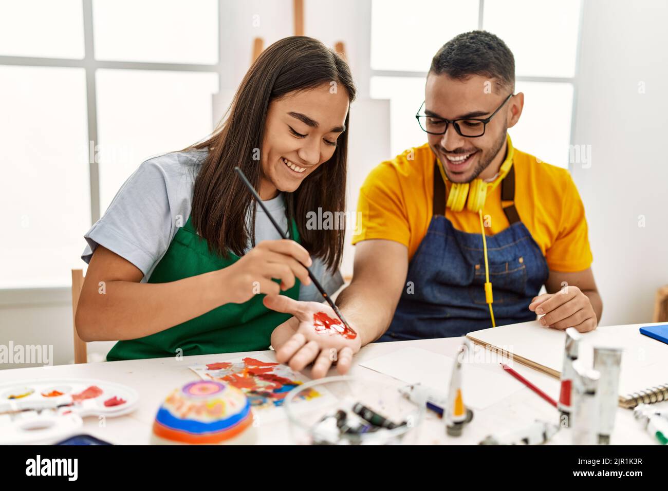 Young hispanic couple smiling happy painting hands sitting on the table ...