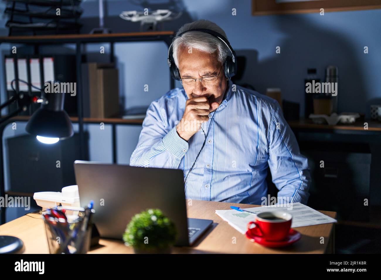 Hispanic senior man wearing call center agent headset at night feeling ...