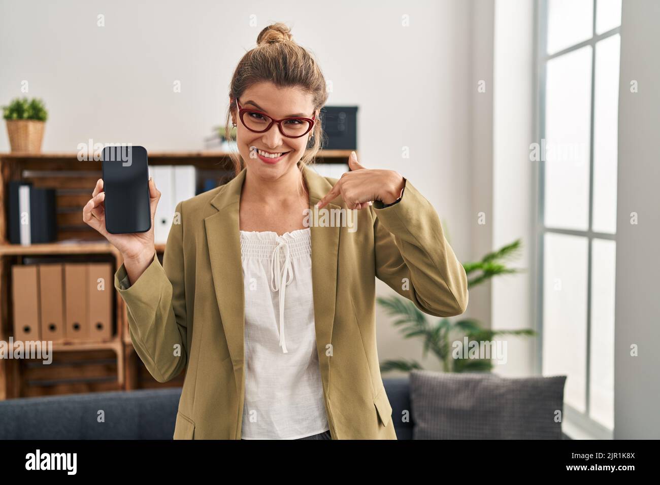 Young woman working at consultation office holding smartphone pointing ...