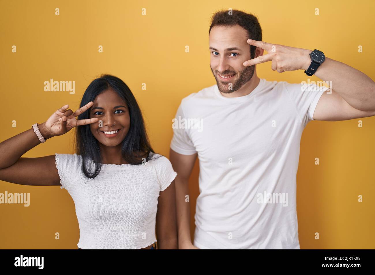 Interracial couple standing over yellow background doing peace symbol ...