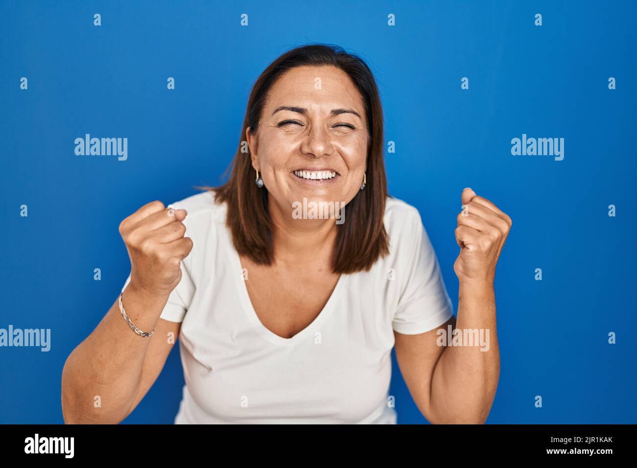 Hispanic mature woman standing over blue background very happy and ...