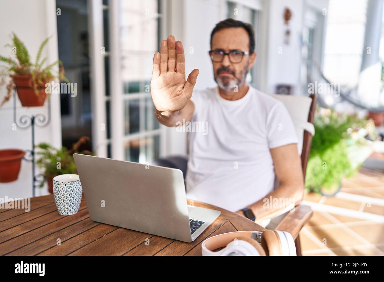 Middle age man using computer laptop at home doing stop sing with palm ...