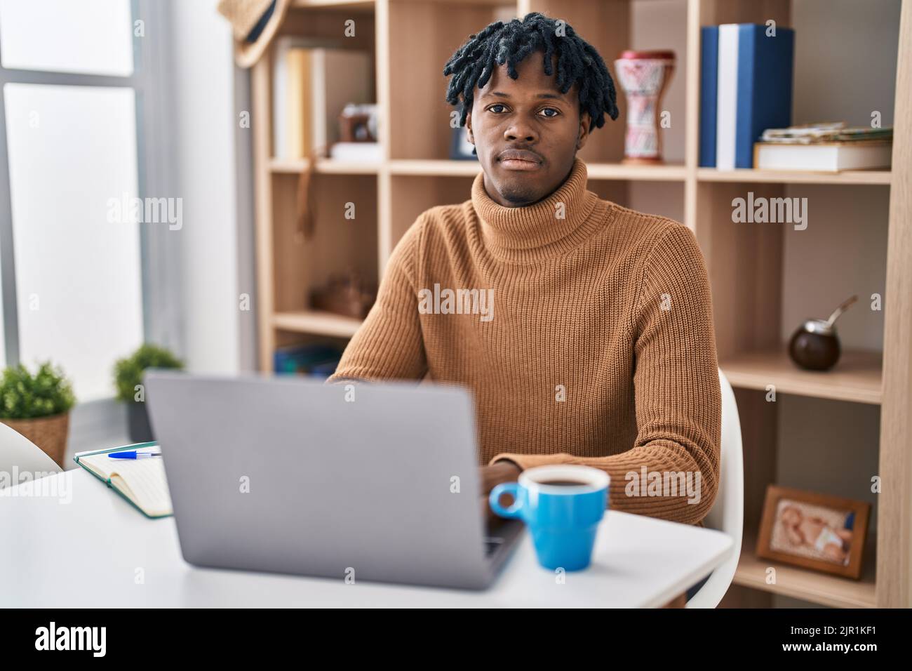 Young african man with dreadlocks working using computer laptop relaxed ...
