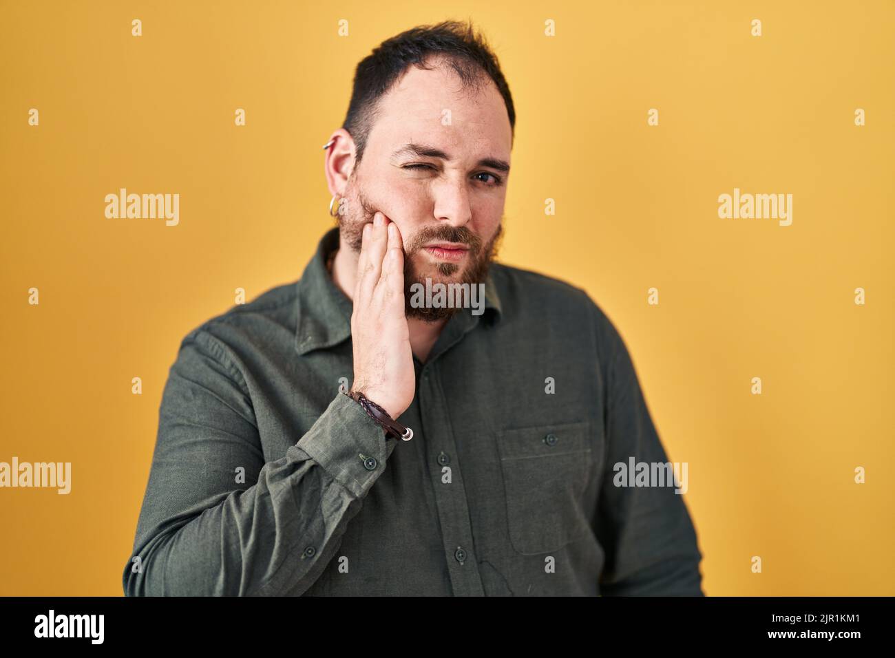 Plus size hispanic man with beard standing over yellow background ...