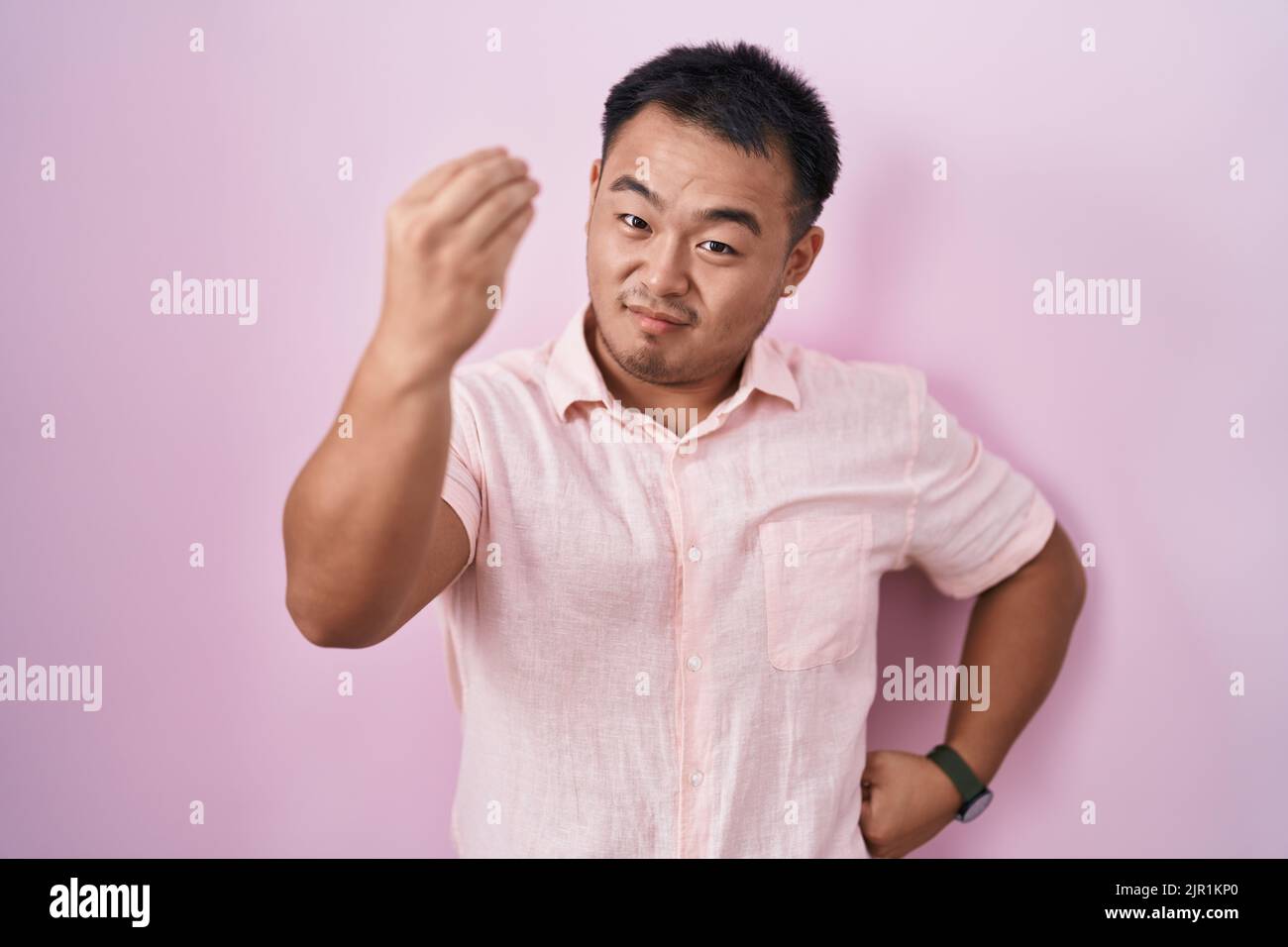 Chinese young man standing over pink background doing italian gesture ...