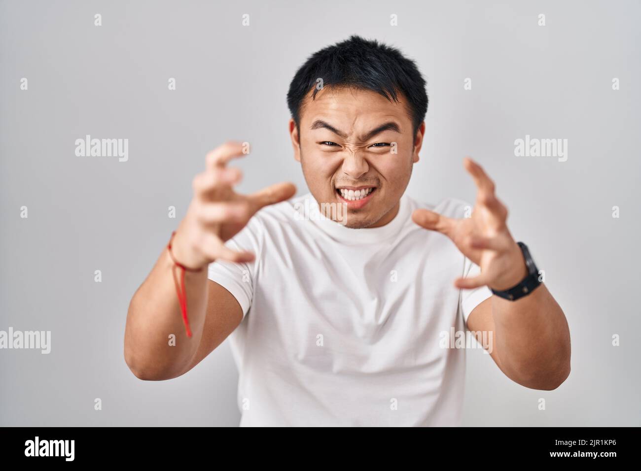 Young chinese man standing over white background shouting frustrated ...