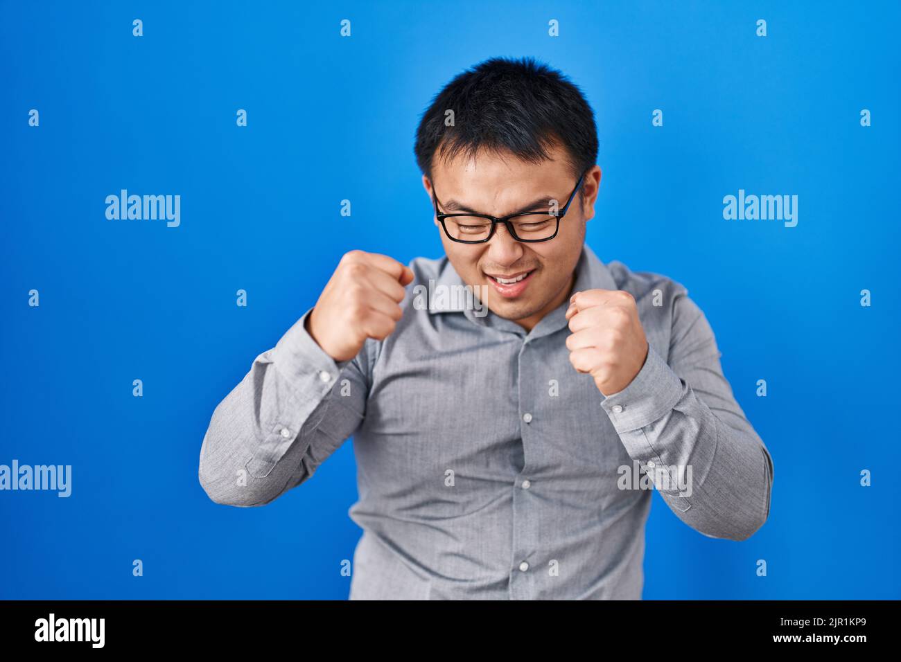 Young chinese man standing over blue background very happy and excited ...