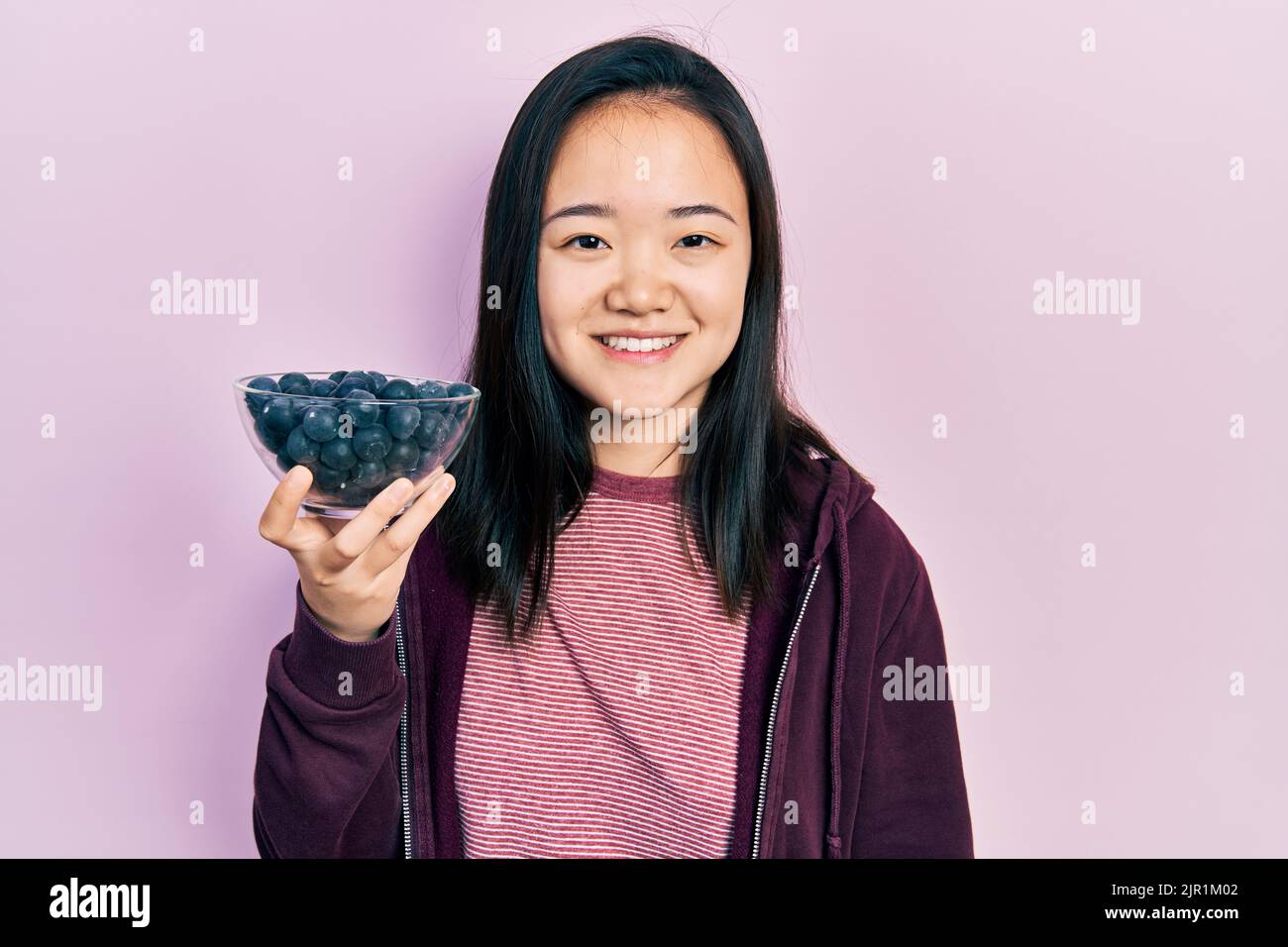 Young chinese girl holding blueberries looking positive and happy ...