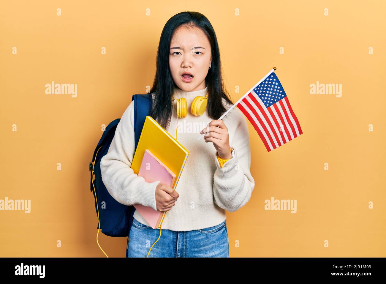 Young chinese girl exchange student holding america flag in shock face ...