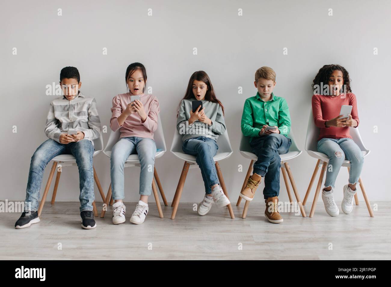 Group Of Amazed Diverse School Kids Using Smartphones Sitting Indoors ...