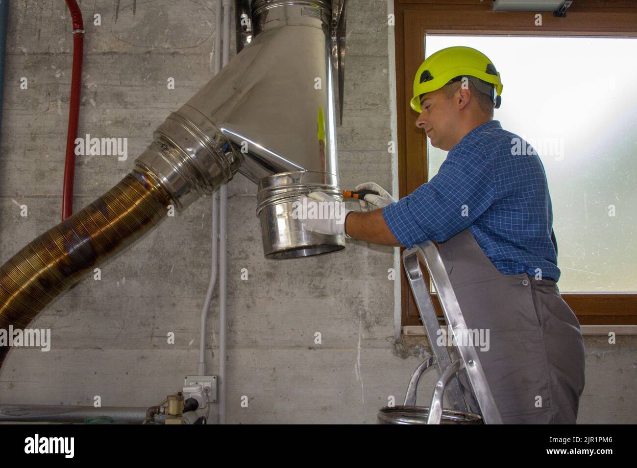 Image of a hard-hatted handyman plumber on a ladder repairing and ...