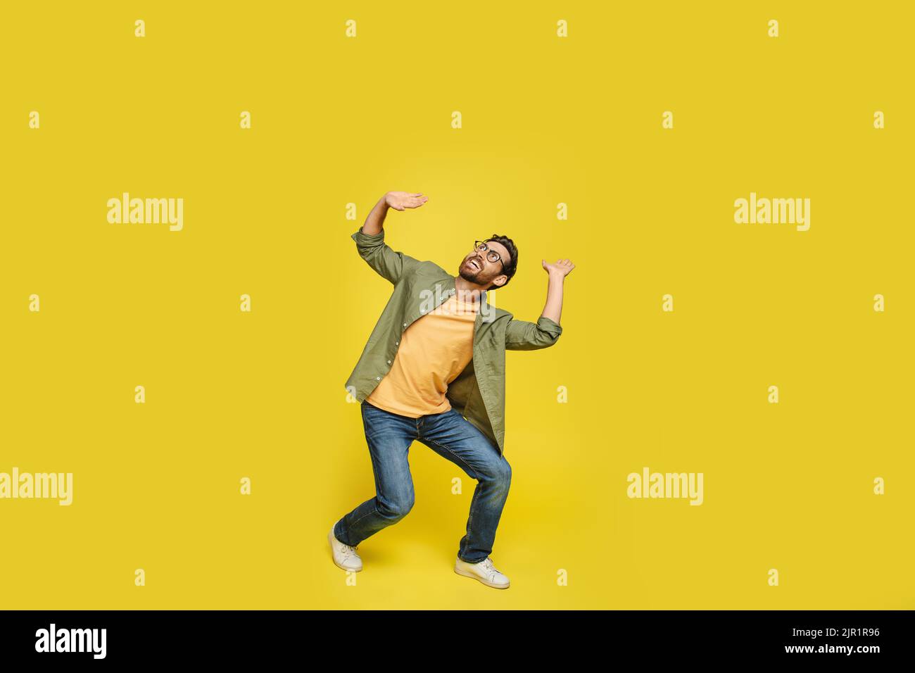 Stylish man holding invisible object overhead posing isolated on yellow ...