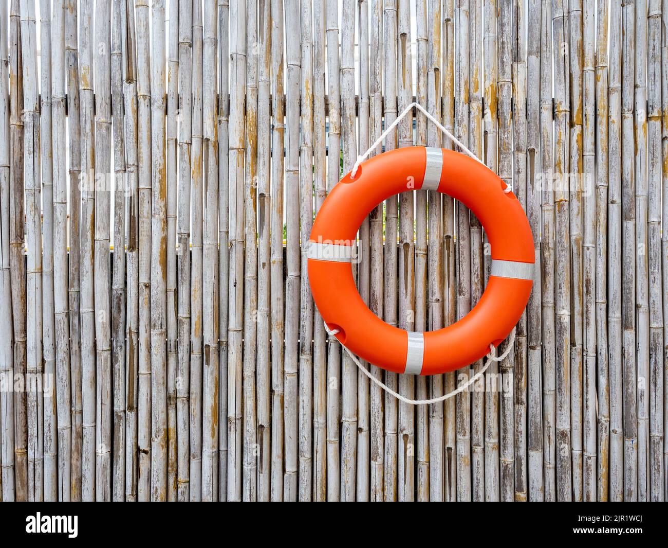 An orange lifebuoy, safety ring hanging on bamboo fence wall background with copy space. Rescue ...