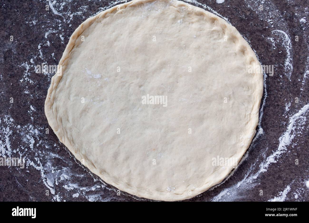 Rolled out pizza dough on floured slate surface, photographed overhead ...