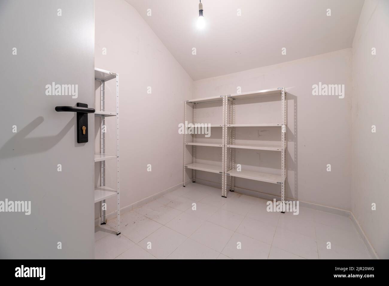 Empty storage room of a house with white metal shelves and gray door ...