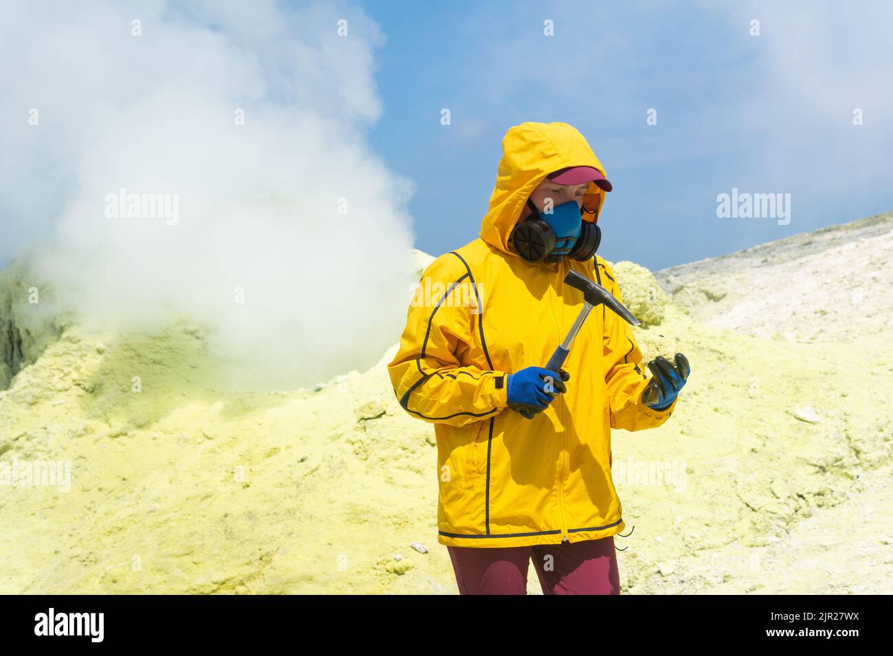 female volcanologist on the background of a smoking fumarole examines a ...
