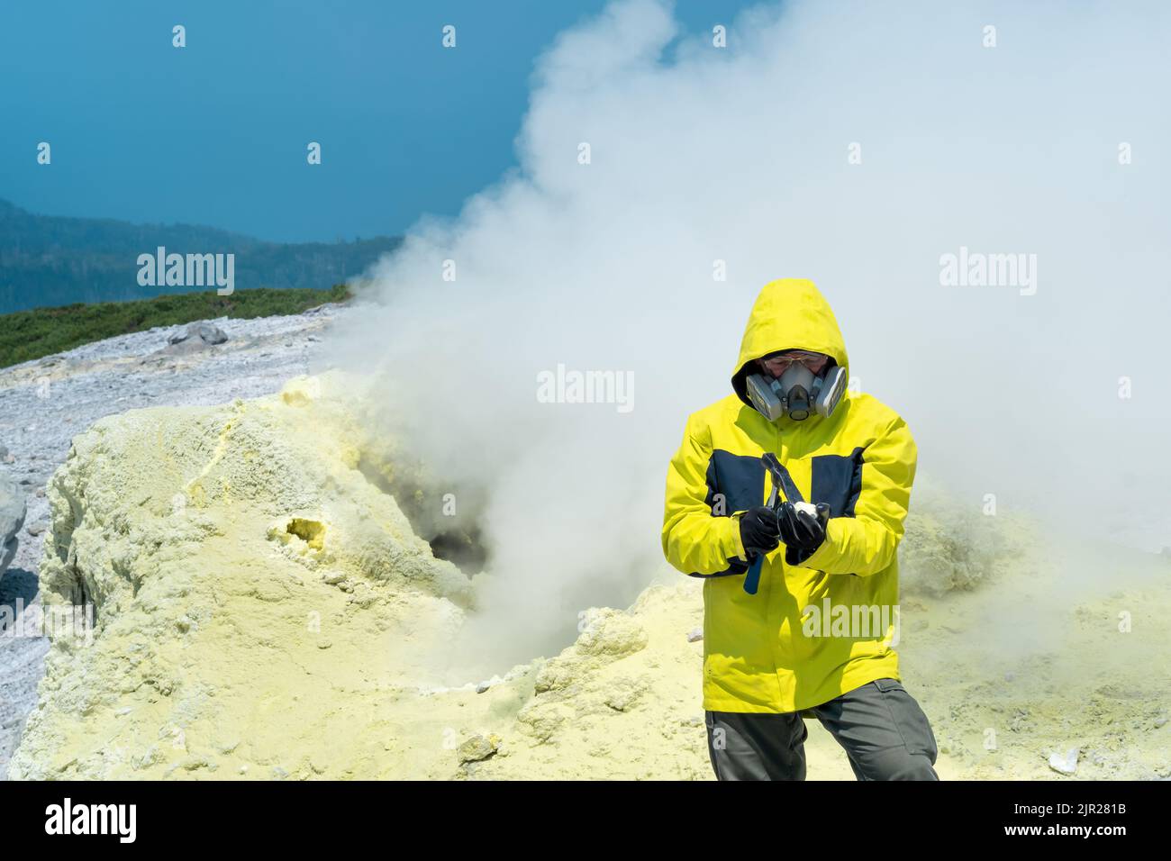 male volcanologist on the background of a smoking fumarole examines a ...