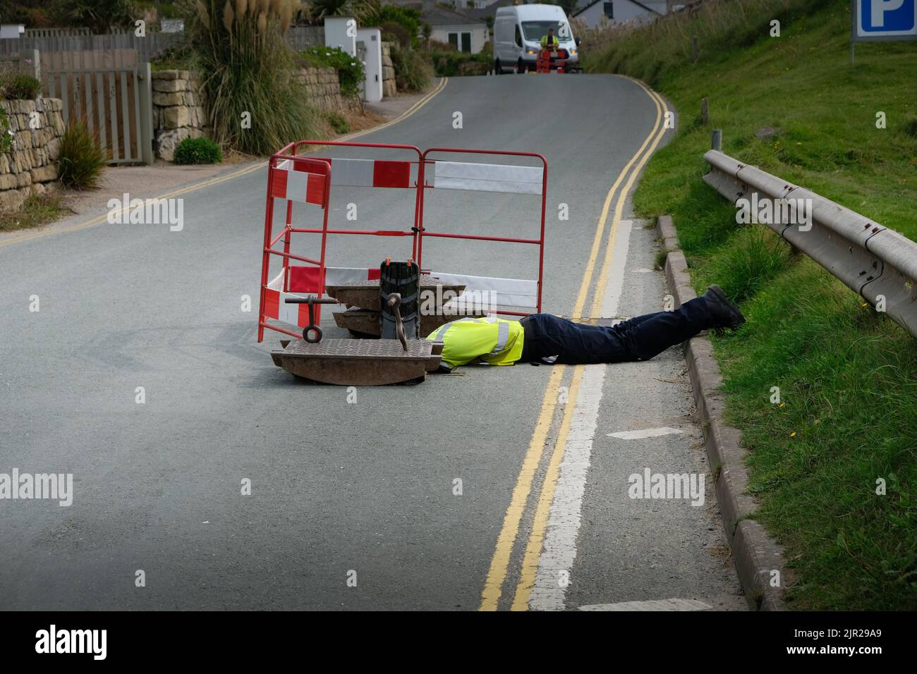 A male utility engineer lays on the road, surrounded by safety barriers ...