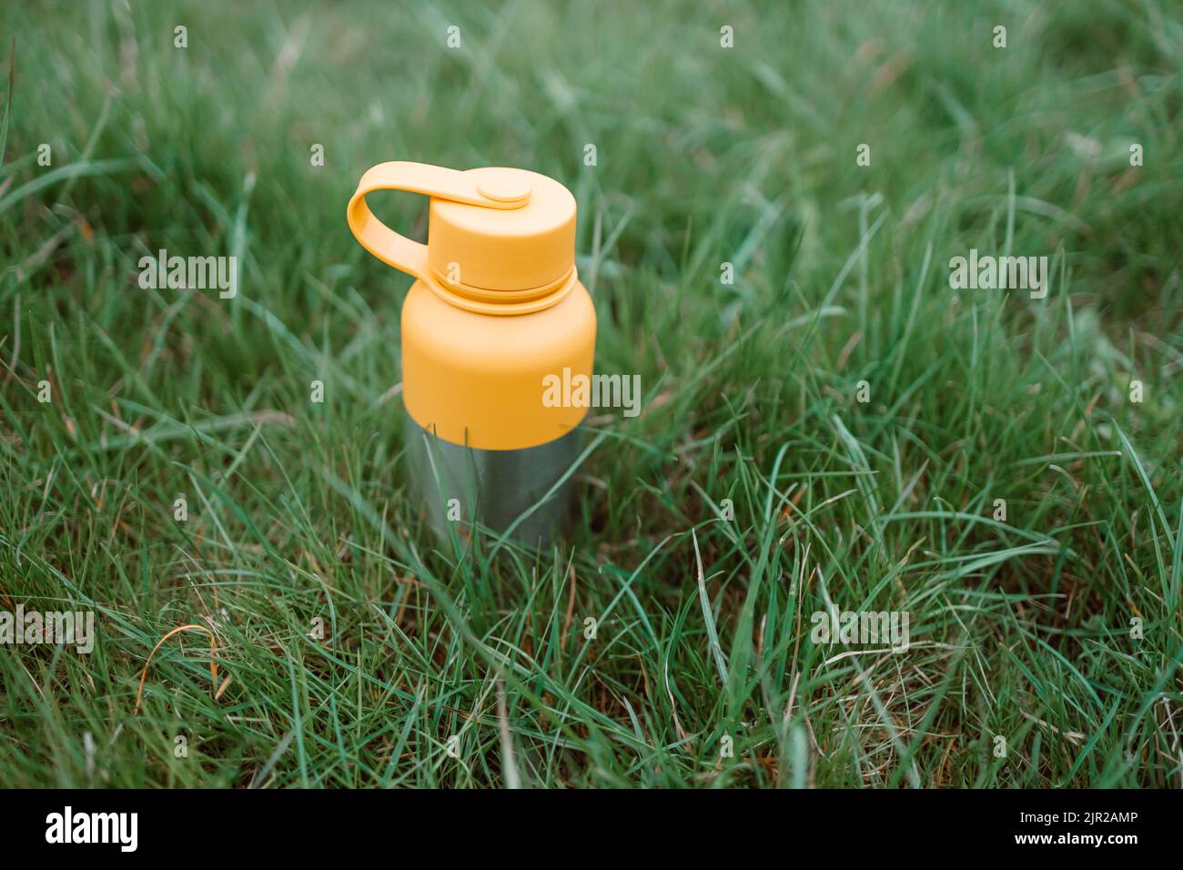 Close-up of steel stainless thermos on green grass with copy space ...