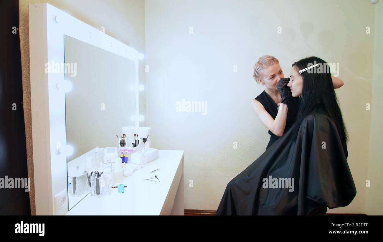 beauty saloon. the cosmetician in black rubber gloves hold tweezers and ...