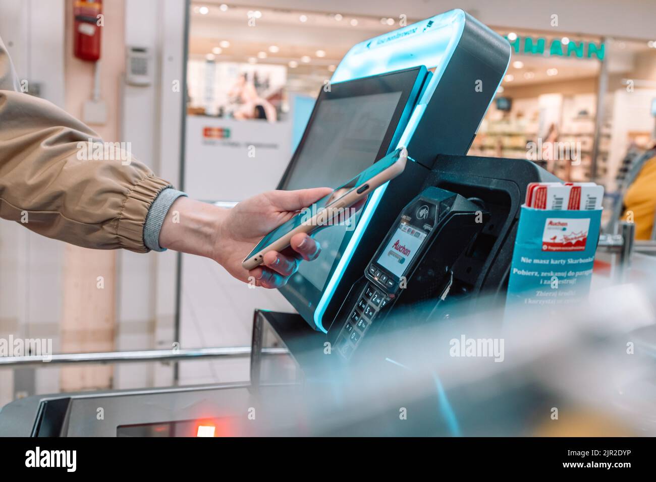 Side view of young woman paying at self-checkout using smartphone app ...