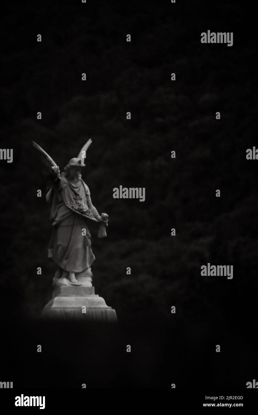 A vertical grayscale shot of stone angel on blur black background Stock ...