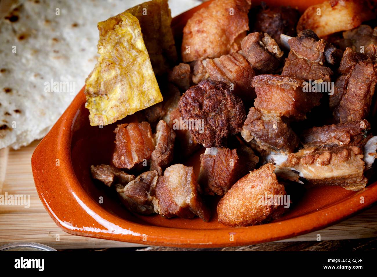 Latin American food of fried meat with plantain and arepas in a clay ...