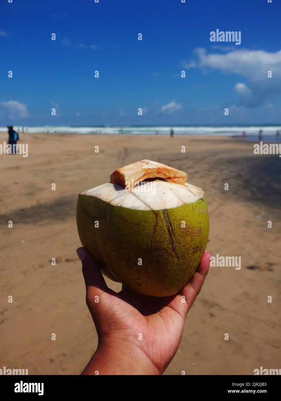 A vertical shot of a male hand holding a cut coconut on a beach Stock ...