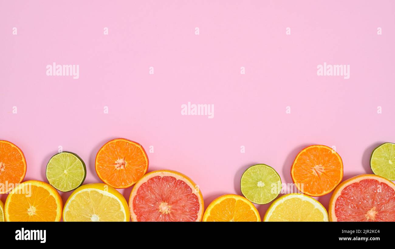 Sliced citrus fruits on bottom of pastel pink background with copy ...