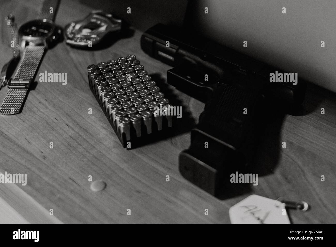 A grayscale of a black gun and steel buckshot with watch on the wooden ...