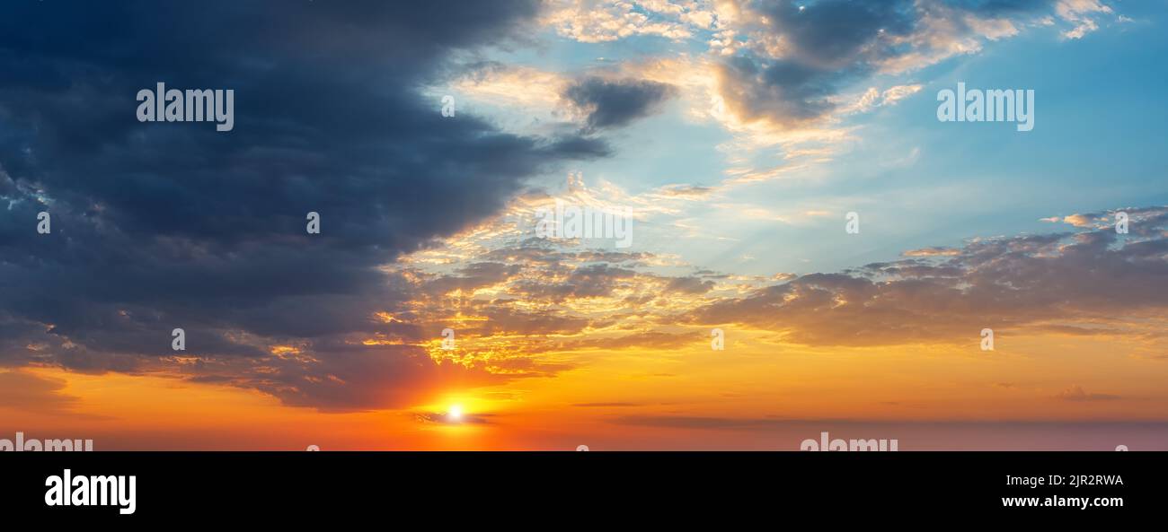 Setting sun in the orange blue evening sky. Sun rays break through the ...