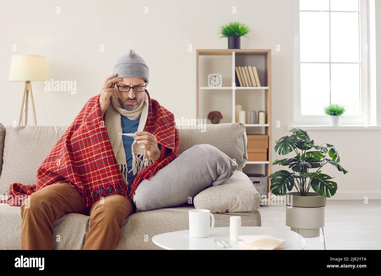 Sick man who has cold or flu sitting on couch at home and looking at ...
