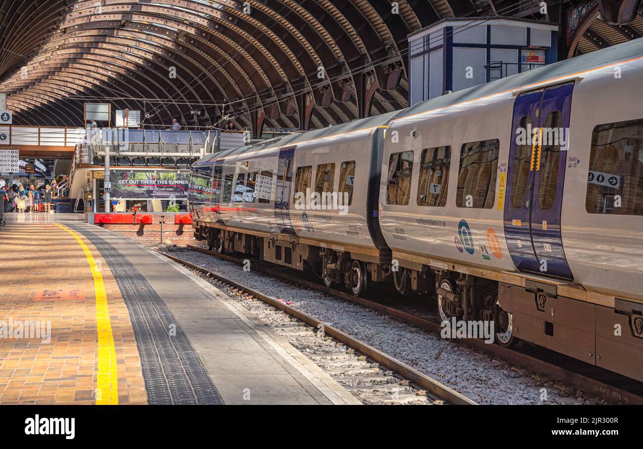 A train rests beside a railway station platform. There are passenger in ...