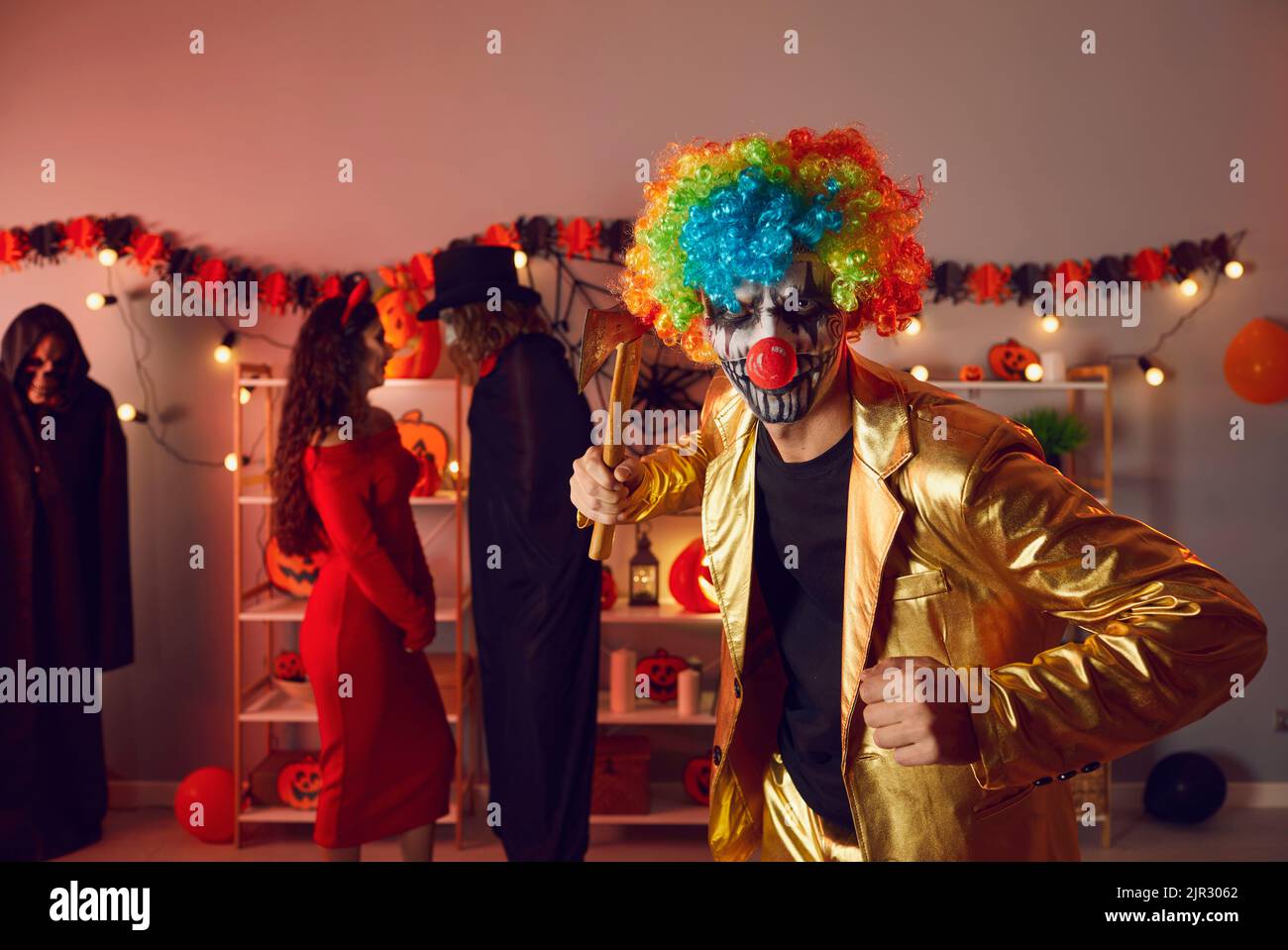 Young man dressed up as spooky evil clown with axe at Halloween party ...